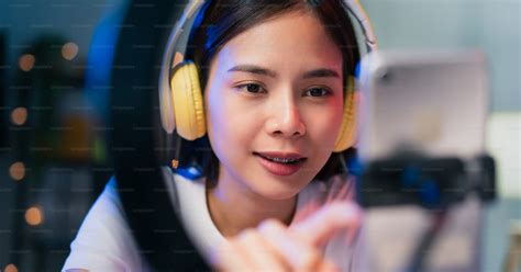 웃고 있는 젊은 아시아 여성은 헤드셋을 착용하고 인터넷에서 생방송을 하고 스마트폰으로 소셜 미디어에서 사람들과 댓글을 읽습니다 사진 Unsplash의 공유 이미지