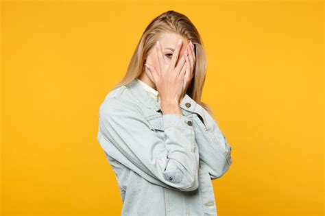 데님 캐주얼 옷에 예쁜 엿보는 젊은 여자의 초상화 스튜디오에서 밝은 노란색 오렌지 벽 배경에 고립 된 손으로 얼굴을 덮고 사람들 라이프 스타일 개념입니다 복사 공간을 모의