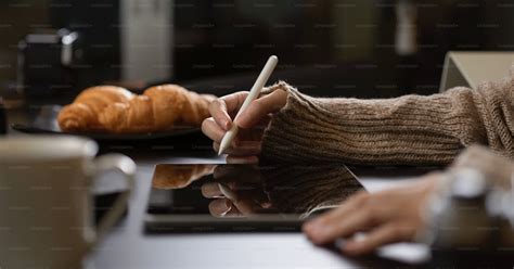 카메라 용품 커피 컵 크로와상이 있는 작업대에서 디지털 태블릿으로 작업하는 여성의 측면도 사진 Unsplash의 태국 이미지