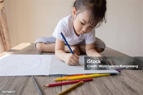 아름답고 사랑스러운 미취학 아동이 나무 테이블에 놓인 흰색 종이에 컬러 연필로 다채로운 그림을 그릴 수있는 위의 사진과 선택적