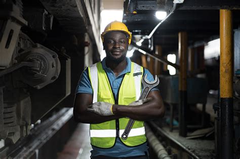 기관차 수리 차고에서 안전 유니폼 헬멧 및 장갑을 착용한 남성 엔지니어 작업자 유지 보수 기관차 엔진의 초상화 남성 철도 엔지니어는 차고에서 렌치 수리 기차 바퀴를