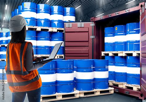 Oil Logistics Woman With Laptop In Warehouse Blue Barrels Near Container Barrels Of Oil On