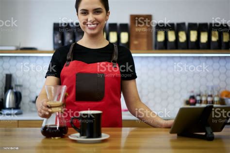 아로마 커피 음료를 만들기 위해 유리 필터를 사용하는 카페의 바에 서 있는 제복을 입은 쾌활한 백인 여성 20대 바리스트의 절반