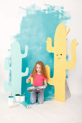 사랑스러운 어린 소녀는 아파트에서 수리를하고 재미 벽을 페인트 스튜디오에서 페인트 롤러와 큰 종이 선인장을 가진 아름다운 웃는 아이의 초상화 즐거운 귀여운 아기 재미 소녀에