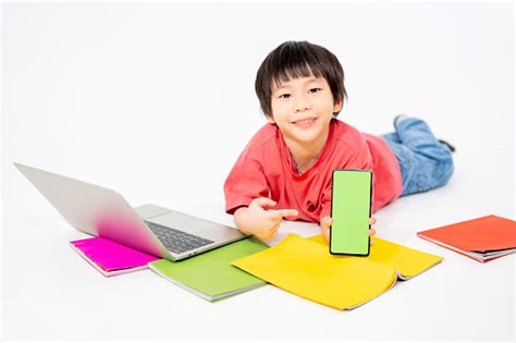 복사 공간 교육 및 기술 개념으로 흰색 배경에 고립 된 노트북과 책으로 바닥에 녹색 화면으로 휴대 전화를 들고 행복한 아시아 소년의 초상화 놀기에 대한 스톡 사진 및 기타