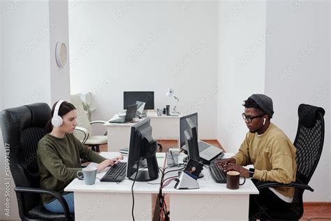 Side View Of Two Young Intercultural Programmers Working In Front Of Computers While Decoding