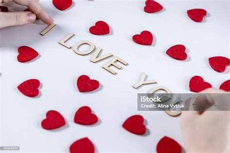 로맨스와 발렌타인 데이를 상징하는 흩어져있는 빨간 펠트 하트로 둘러싸인 흰색 배경에 I Love You를 철자하는 나무 글자를 배열하는 사람 2월에 대한 스톡 사진 및 기타
