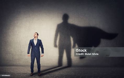 단호한 사업가는 영웅 자세에 자신감을 갖고 뒤에 벽에 용감한 슈퍼 히어로 그림자를 투사합니다 비즈니스 리더십 과 동기 부여 개념 야망과 힘 기호 슈퍼히어로에 대한 스톡 사진