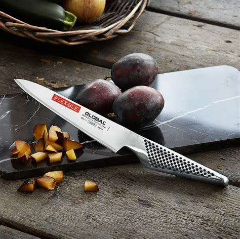 Global Knife Universal Flexible Knife On A Wooden Surface Beside A Sliced Fruit