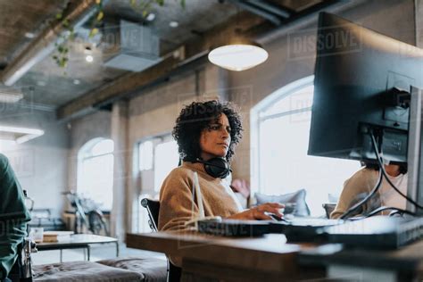 Female Hacker With Wireless Headphones Around Neck Using Computer While Working In Office