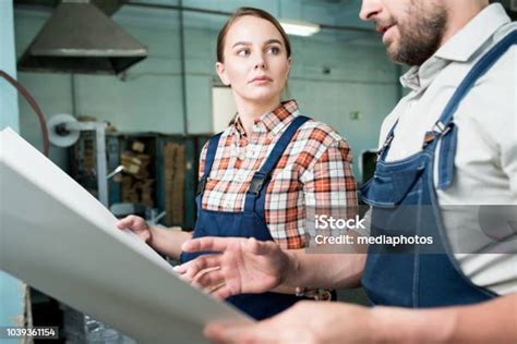 그들은 공장에서 청사진을 논의 하는 동안 동료에 게 조용히 듣고 체크 무늬 셔츠에 심각한 레이디 엔지니어 검사 보기에 대한 스톡 사진 및 기타 이미지 Istock