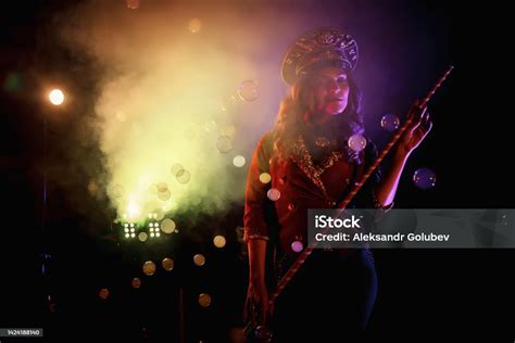 지팡이를 가진 서커스의 여성 마술사 환상 주의자가 검은 색 배경에서 비누 거품을 보여줍니다 무대 의상에 세련된 모자를 쓴 연극복을 입은 여성 여배우 극장 공연의 개념 서커스