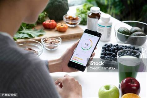 여성 아시아 전문 영양사는 다양한 과일 견과류 채소 및 건강 보조 식품이 있는 전화기에서 데이터를 확인하고 작업하느라 바쁩니다 휴대폰 앱에 대한 스톡 사진 및 기타 이미지