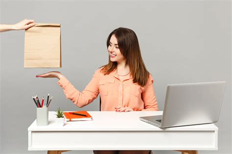 테이크 아웃에 대 한 갈색 맑은 빈 빈 공예 종이 가방에 손을 가리키는 젊은 쾌적 한 여자 회색 배경에 고립 된 Pc 노트북 책상에서 작업을 앉아 성취 비즈니스 커리어