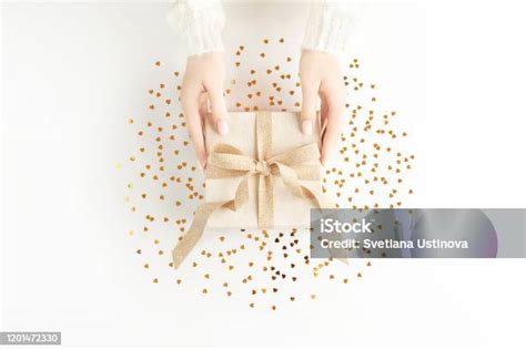 따뜻한 흰색 스웨터와 아름다운 흰색 매니큐어 골드 심장 Sheped 반짝반짝 흰색 배경에 우아한 황금 활과 현재 상자를 들고 여성 손 휴일축제 배경 플랫 레이 스타일입니다