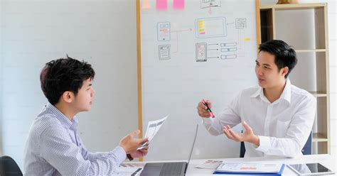 두 명의 아시아 남성이 휴대 전화에서 웹 사이트와 응용 프로그램을 디자인하기 위해 함께 일하고 있습니다 사진