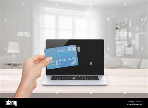 Hand Holding Credit Card Against Laptop Backdrop Symbolizing Online Payment Convenience