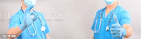 파란색 유니폼과 회색 배경에 의료 장갑을 끼고 있는 두 명의 의사 또는 의료진이 서로 마주치며 엄지손가락을 위로 또는 좋아하며
