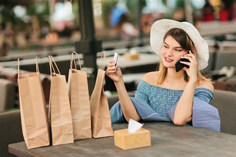 온라인 쇼핑 전화로 이야기하고 그녀의 손에 은행 카드를 들고있는 동안 야외 카페에 앉아 쾌활한 젊은 쇼핑 중독자 여자 가방에 대한 스톡 사진 및 기타 이미지 Istock