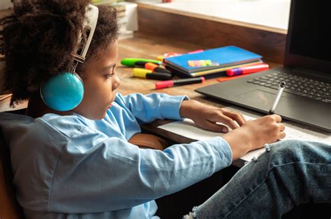 아프리카 계 미국인 소녀는 숙제를하고 메모를하고 집에서 헤드폰과 노트북을 사용합니다 학교 개념으로 돌아 가기 가정에서의 학교 원격 교육 홈 스쿨링 전자 학습 다양한 사람들