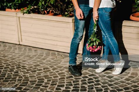 청바지 바지와 신발에서 여자와 남자 다리의 하단 클로즈업 사진 보기 꽃의 꽃다발을 가진 소녀는 발 끝에 서 있고 데이트 중에 키스 하는 세련 된 커플 연인 야외 청바지에