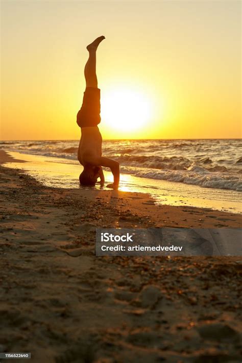 열대 섬의 아름다운 황금 빛 해변에서 여름 요가 세션에서 젊은 남자가 균형 아사나 연습 살람바 시르사나를 하는 남자는 일출에 헤드스탠드를 지지했습니다 해변에서 명상에