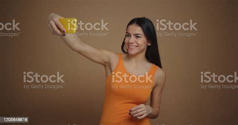 갈색 배경에 고립 된 스마트 폰에서 셀카를 찍는 쾌활한 미소 짓는 여성 갈색에 대한 스톡 사진 및 기타 이미지 갈색 갈색 머리 긍정적인 감정 표현 Istock