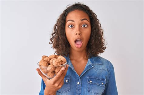 고립 된 흰색 배경 위에 서 있는 호두와 함께 그릇을 들고 있는 젊은 브라질 여성은 깜짝 얼굴로 충격에 무서워하고 두려움과 두려움 표현으로 흥분했습니다 감정에 대한 스톡