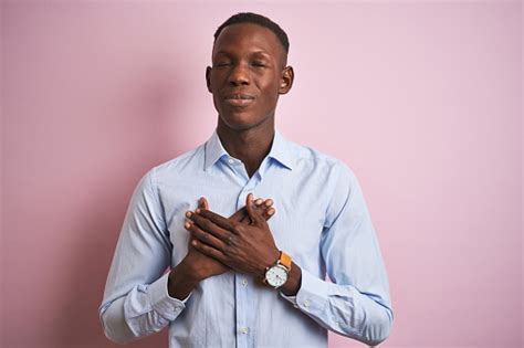 파란 우아한 셔츠를 입은 아프리카계 미국인 남성이 고립된 분홍색 배경 위에 서서 가슴에 손을 얹고 얼굴에 감사하는 제스처를 취했습니다 건강 개념 감사에 대한 스톡 사진 및