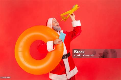 고무 반지 여권 종이 비행기를 들고 산타 클로스 의상을 입고 회색 수염을 가진 흥분 된 노인의 측면 보기 미래의 여행을 기쁘게 30 34세에 대한 스톡 사진 및 기타 이미지