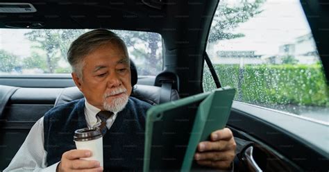 자동차 뒷좌석에 앉아 뜨거운 커피를 마시며 디지털 태블릿으로 사업 계획을 읽는 동안 자신감 있는 수석 사업가 자동차 운전에