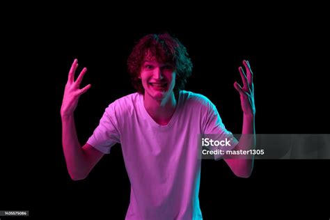 화가 난 것 같습니다 보라색 네온 빛으로 어두운 배경에 고립 된 부정적인 얼굴 표정을 가진 청년의 절반 길이의 초상화 20 24