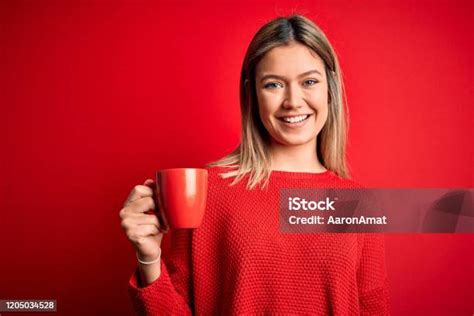 행복한 얼굴 서서 치아를 보여주는 자신감 미소와 함께 고립 된 빨간 배경 위에 서있는 커피 잔을 마시는 젊은 아름다운 여성 마시기에 대한 스톡 사진 및 기타 이미지 Istock