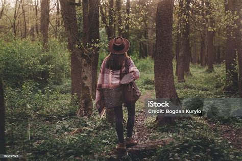 저녁 햇살에 숲에서 걷는 배낭 모자에 세련 된 Hipster 여행자 소녀 보헤미안 유행 여자 햇빛에 탐험입니다 텍스트를 위한 공간입니다 대기 순간입니다 방 랑 벽 가을에