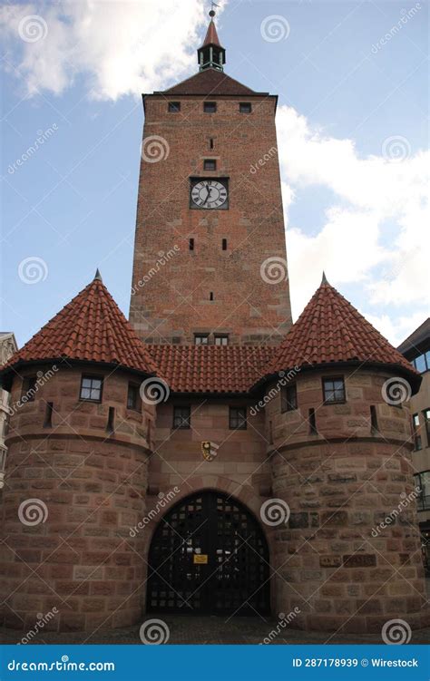 A Large Clock Tower In The Middle Of An Alley Near Buildings Stock