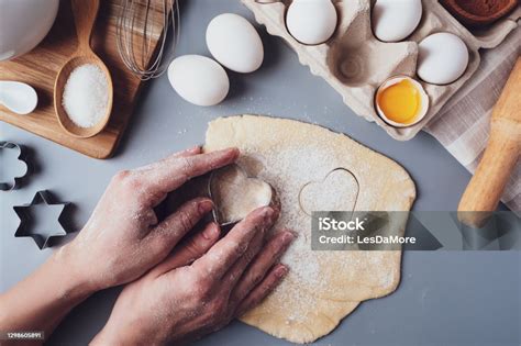 소녀는 회색 배경에 심장 평평한 평신도 구성의 모양으로 쿠키를 준비합니다 쿠키 커터와 반죽을 여성의 손에 들어놓습니다 발렌타인 데이 아버지의 날 어머니의 날 을위한 음식의