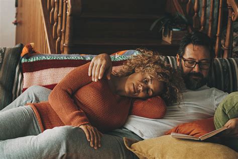 집에서 시간을 즐기고 소파에 누워 함께 휴식을 취하는 남자와 여자 커플 남편은 책을 읽고 아내는 그에게 자고 있습니다 일요일 레저 활동 실내 개념 라이프 스타일 사랑과