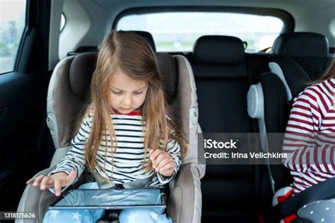 어린 소녀 자매는 자동차에서 운전하고 아이들은 태블릿과 휴대 전화에서 비디오 게임을합니다 아이 벨트가있는 안전한 유아용 좌석으로