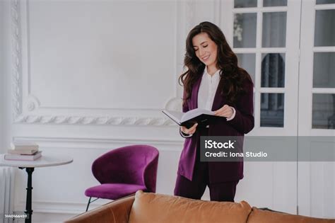 노트북을 들고 있는 쾌활한 갈색 머리 사업가 보라색 양복을 입고 일주일을 계획하고 있다 일기에서 그녀의 의제를 보는 성공적인 학생 법률 책을 들고 있는 아름다운 변호사