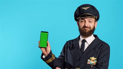 Jeune aviateur utilisant un écran vert habillé en capitaine montrant un smartphone avec un