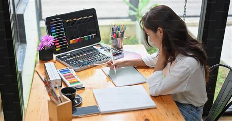 스튜디오에서 캔버스 포스터에 그림을 그리기 전에 디지털 태블릿에서 그림 레이아웃을 스케치하는 여성 예술가 나무 테이블에 색칠 용품 사진 Unsplash의 테이블 이미지