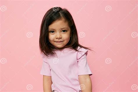 A Little Beautiful Girl Of Preschool Age Stands On A Pink Background In