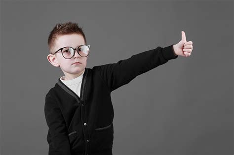 같이 안경을 쓰고 카메라를 향해 웃고 엄지손가락을 치켜들고 있는 어린 여학생의 초상화가 시원한 승인 기호를 보여주고 있습니다 실내 스튜디오는 회색 배경에 고립 촬영 복사