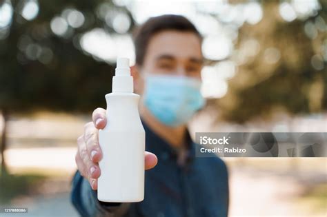 파란색 멸균 의료 마스크의 남자는 방부제흰색 플라스틱 병을 보여줍니다 코로나바이러스 를 보호하기 위해 살균 스프레이를 사용하여