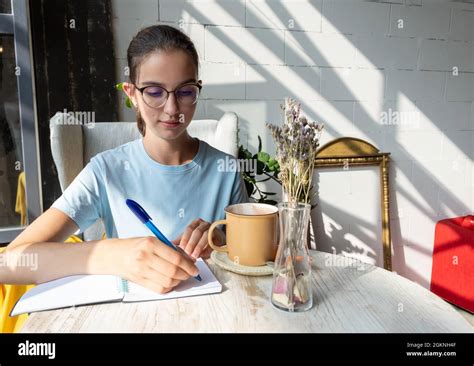 Pensive Girl Student Writes With A Pen An Assignment In A Notebook