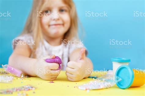 금발의 소녀는 파란색 배경에 고립 된 보라색 점액을 보유하고 있습니다 점액 장난감을 가지고 노는 아이 점액 만들기 공간을