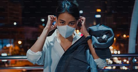 패션 사무복을 입은 성공적인 젊은 아시아 사업가는 의료용 안면 마스크를 쓰고 웃으며 카메라를 바라보며 도시의 현대 도시의 밤에