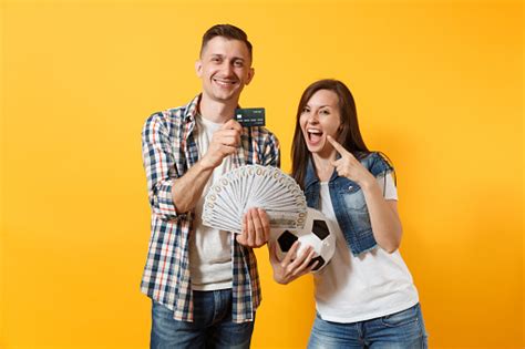 젊은 승 커플 여자 사람 축구 팬 들의 달러 돈 신용 카드 축구공 번들을 들고 노란색 배경에 고립 된 지원 팀을 응원 합니다