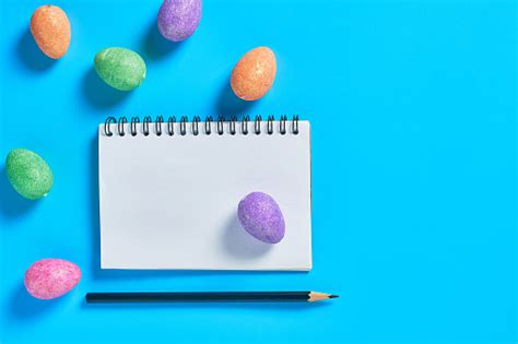 많은 사람들이 검은 연필 과 메시지를 위한 빈 종이 메모장 근처 반짝이 흩어져 다채로운 계란 부엌에 파란색 책상에 놓여있다 부활절 개념입니다 텍스트의 공백입니다 맨 위 보기