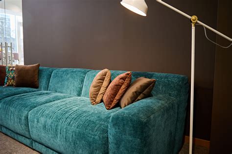 가구 상점의 쇼룸에서 현대적인 세련된 살이 포동 포동 가구의 전시 갈색 벽 배경에 램프에 의해 조명 청록색 부드러운 벨루어 소파와 갈색 베개의 클로즈업 0명에 대한 스톡